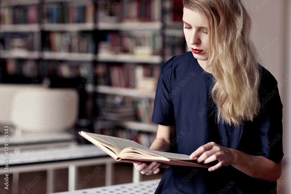 Caucasian blonde woman reading a book in a public modern library. Red ...