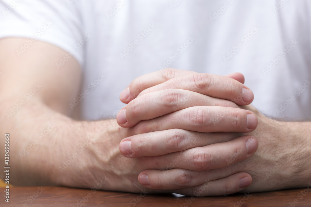 Man is sitting and holding his hands together on a wooden table. Like ...
