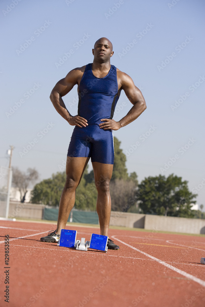 Full length of African American male athlete at starting block on race ...