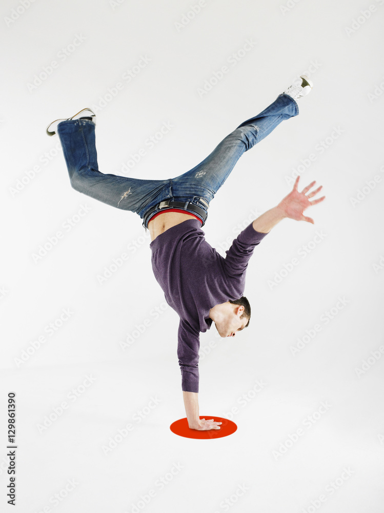 Full length of a young man doing one handed handstand on red dot ...