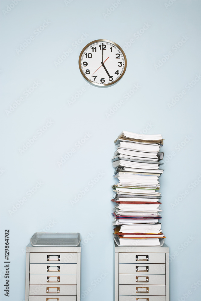 Office wall with clock stack of paperwork in outbox on file cabinet ...