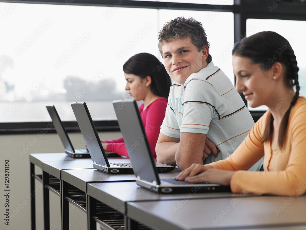 Portrait of teenage boy with female classmates using laptops in ...