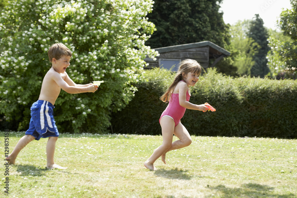 Full length side view of a boy shooting girl with water pistol in the ...