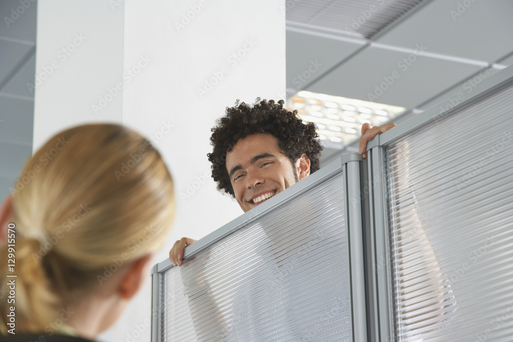 Smiling male office worker peering over cubicle wall to greet blond ...