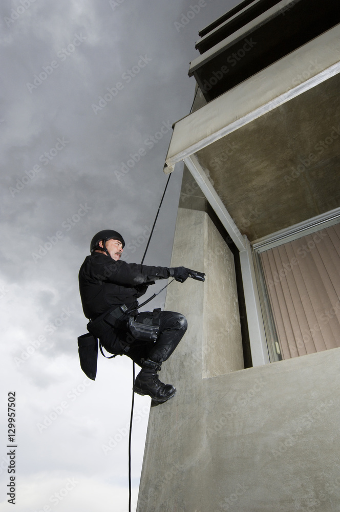 SWAT team officer aiming handgun through window while rappelling ...