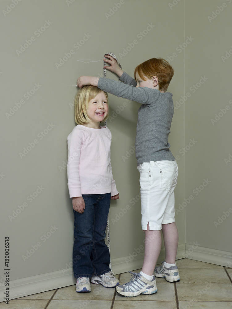 Full length of two girls measuring height difference against wall Stock ...