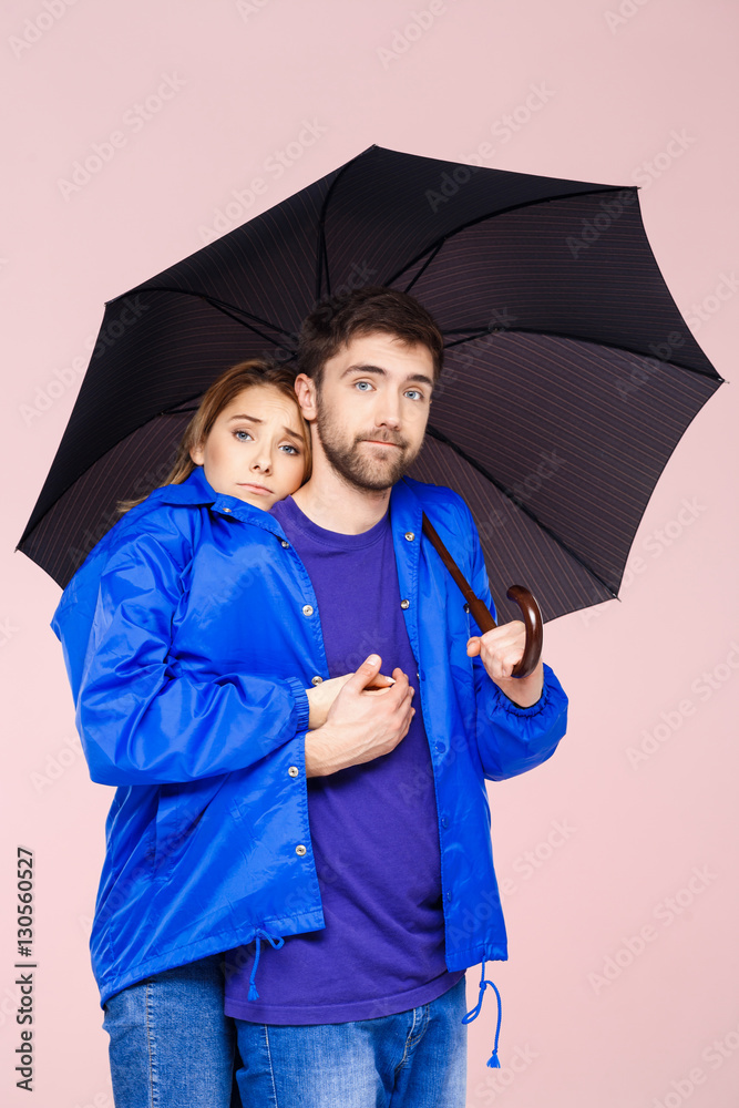 Young beautiful couple posing wearing one rain coat holding umbrella ...