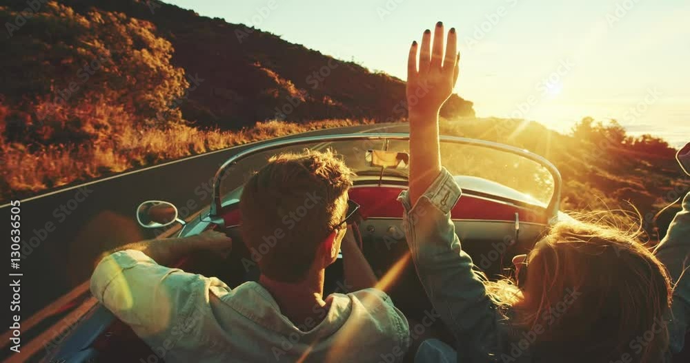 Happy couple driving on country road into the sunset in classic vintage ...