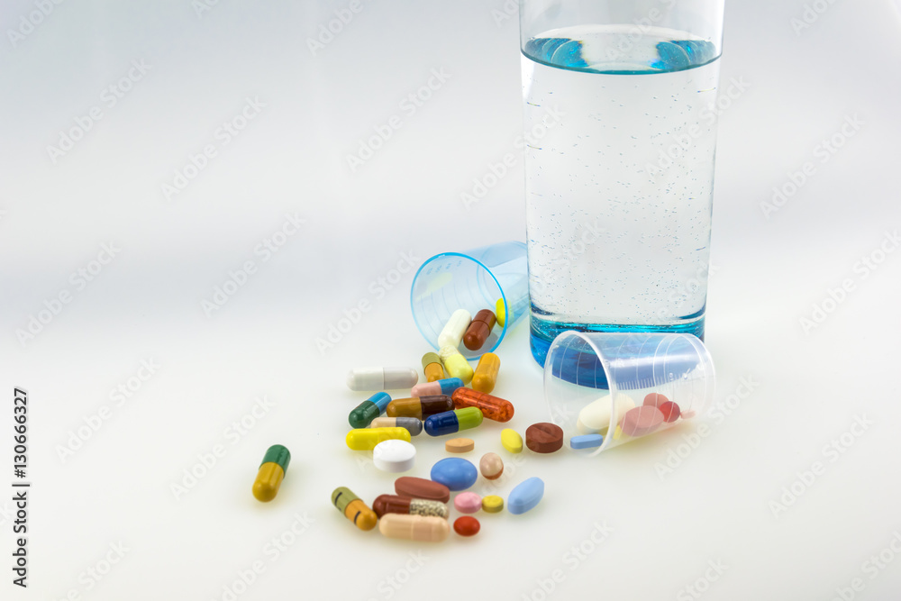 Many colored tablets and capsules near a glass of water with blue ...
