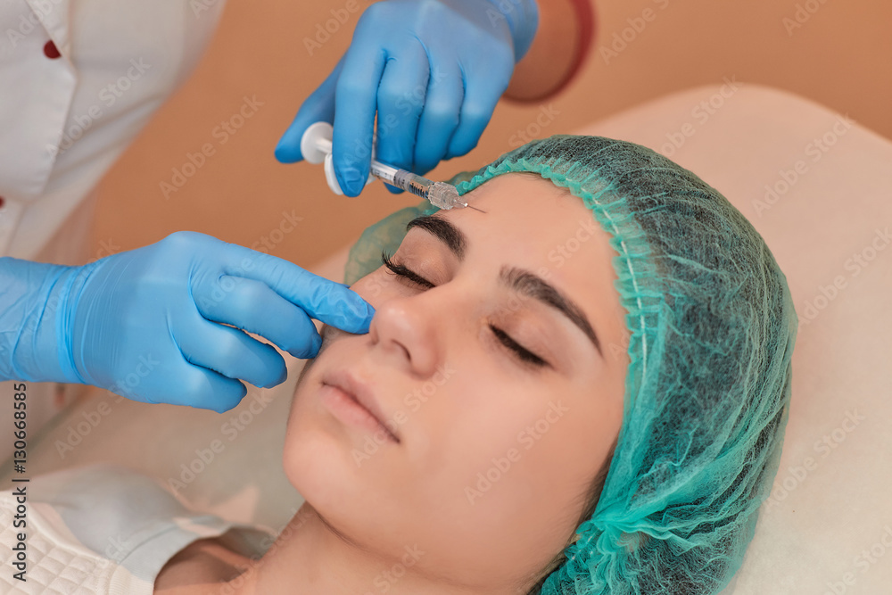 Hands of cosmetologist making injection in face. Young woman gets ...