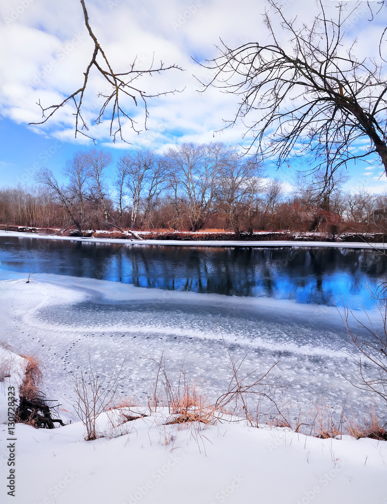half-frozen river and the coast in the snow in a winter sunny day ...