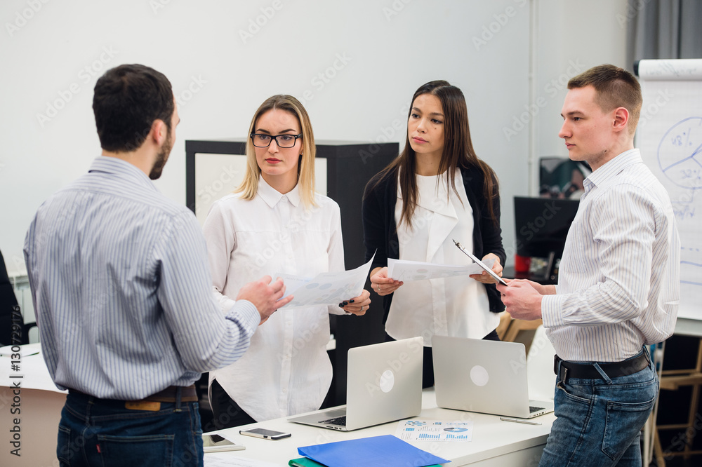 Four young business people working as a team gathered around laptop ...