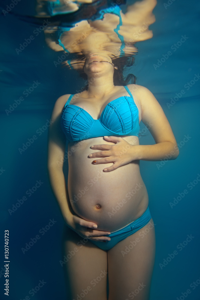Pregnant woman in bikini underwater in blue background shows off your belly. Portrait. Vertical ...