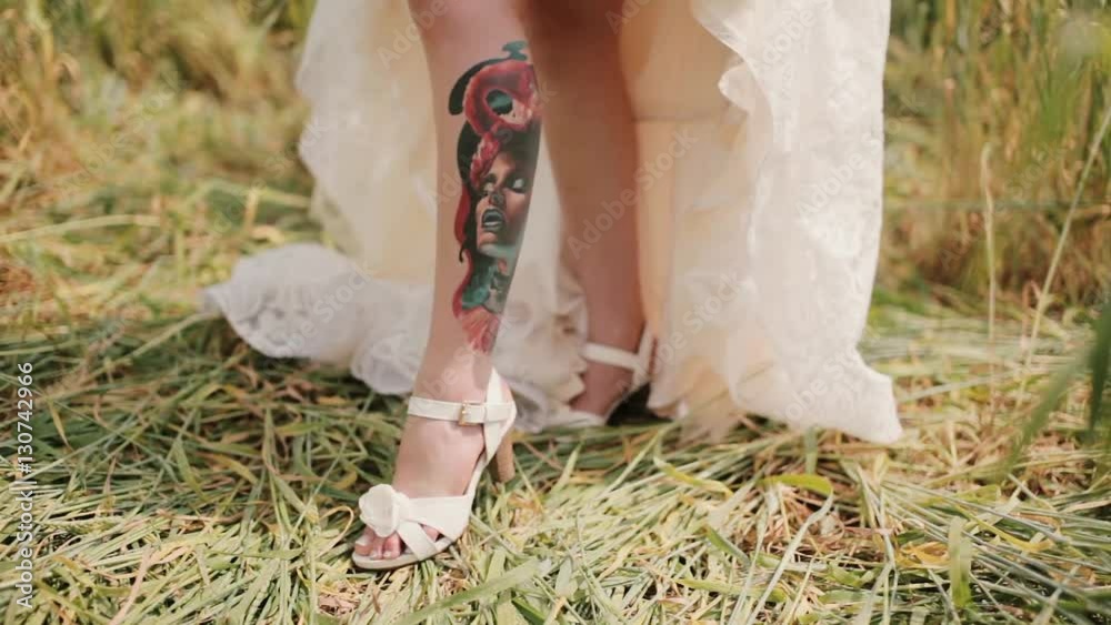 Bride shows a tattoo on her leg under a wedding dress. Surprising view ...