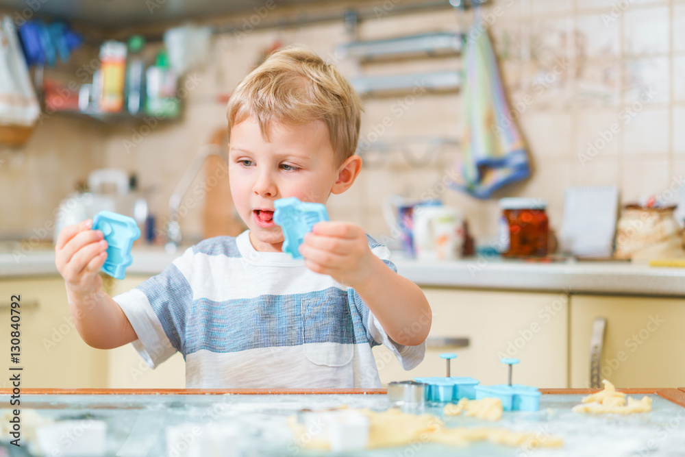 Little blond kid plays with molds for making ginger biscuits or cookies ...