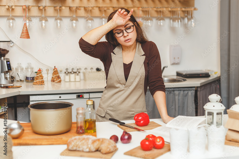 Young brunette housewife in the kitchen is tired cooking tomato soup ...