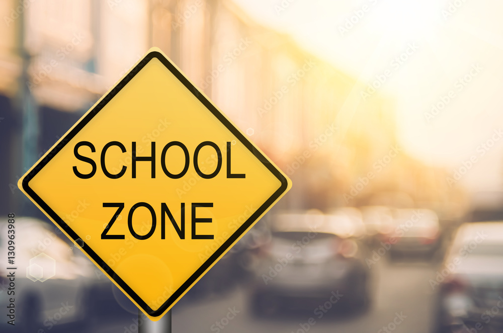 School zone warning sign on blur traffic road with colorful bokeh light abstract background ...