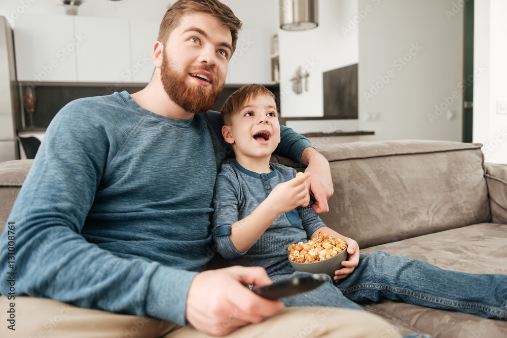 Cheerful father watching TV with his cute son holding popcorn. Stock ...