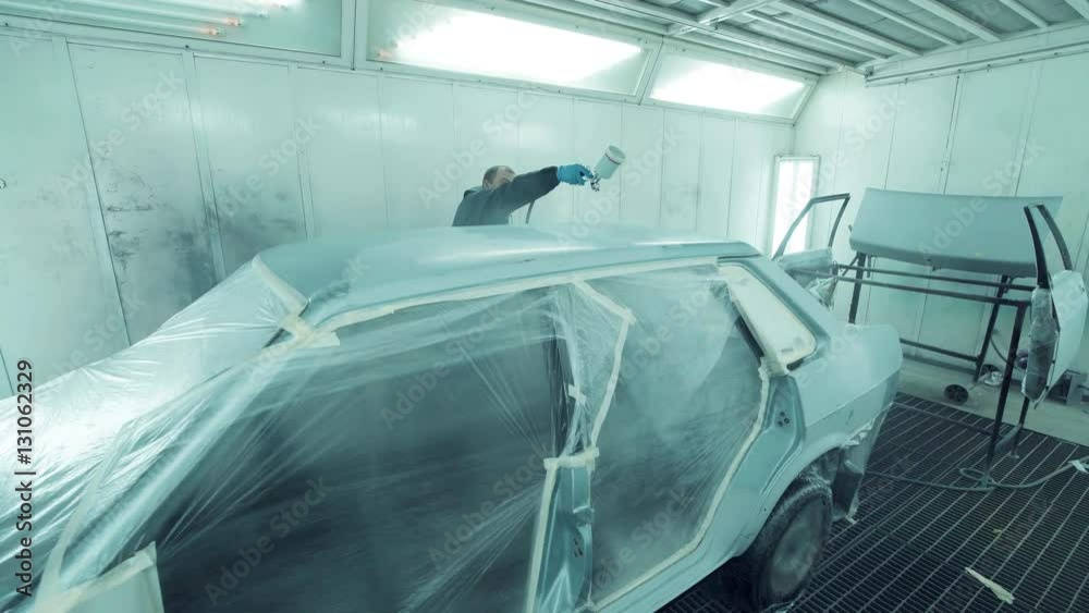 Mechanic spray painting a car in a body shop with a canister of white ...