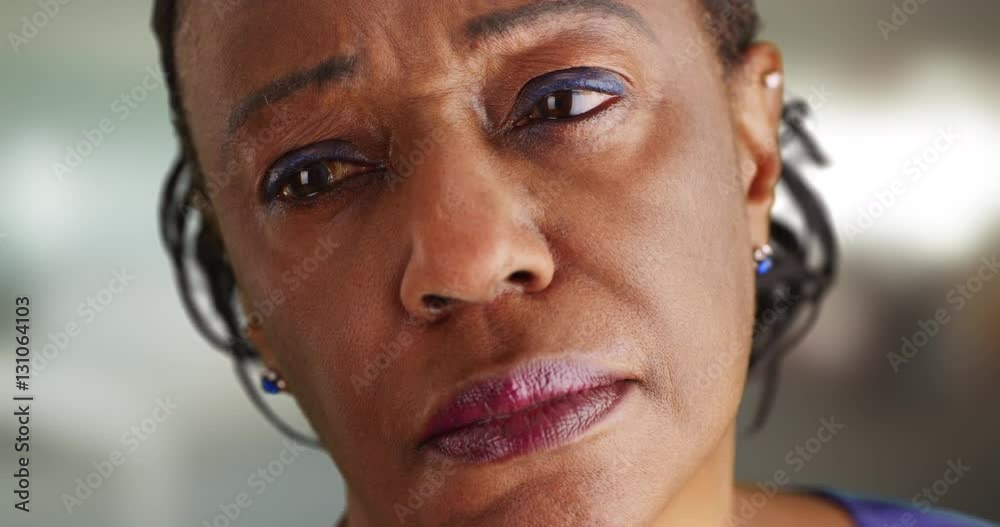 A close-up of a elderly black woman looking off in the distance sadly ...