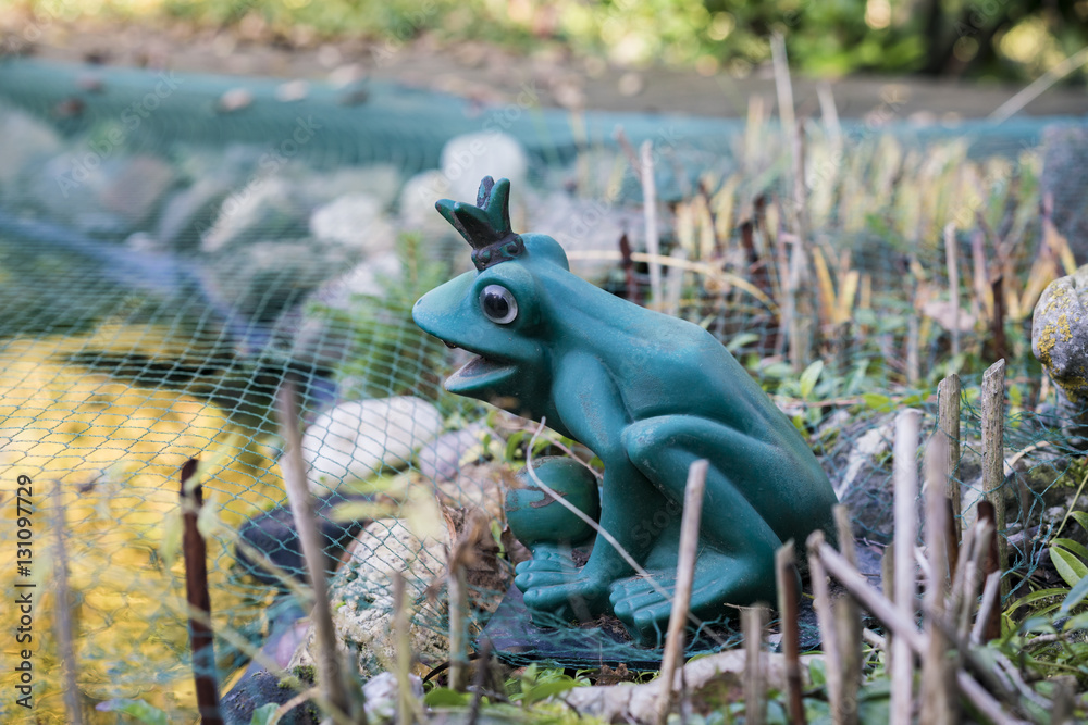 Close up view of frog garden statue wearing crown placed on rock mound ...