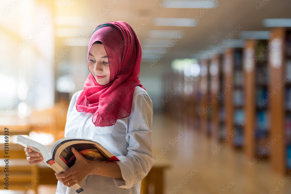 Beautiful Muslim girl reading book with hijab on blur library ...