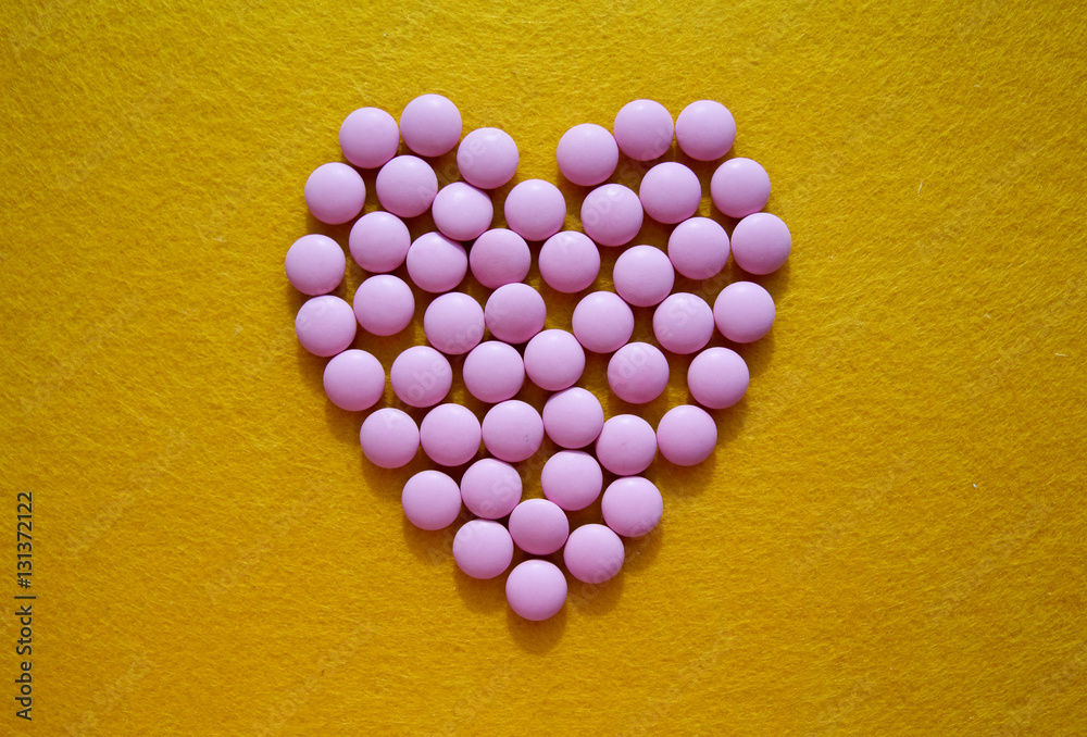 heart made of pink pills on bright yellow felt background. Stock Photo ...