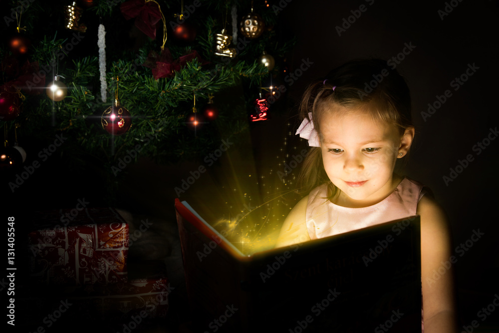 little girls reading a magical Christmas book by a Christmas tree in ...