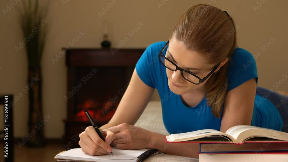 Beautiful college student in glasses lying on sofa and studying. Making ...