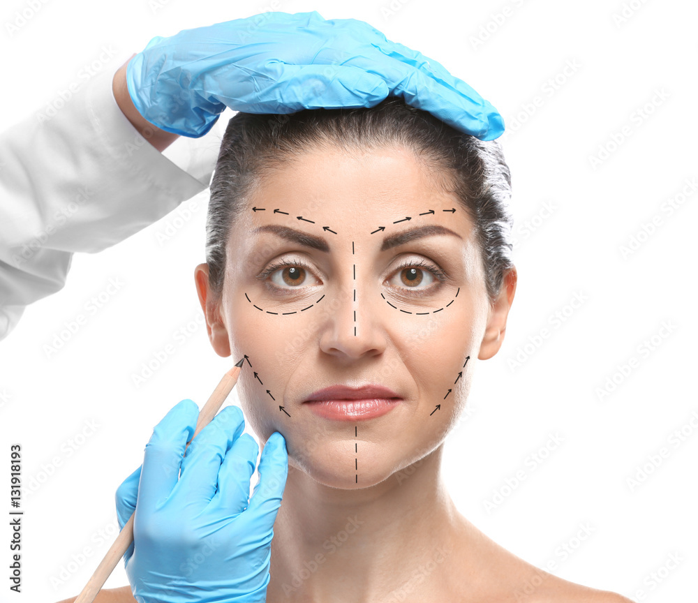 Surgeon drawing marks on female face against white background. Plastic ...