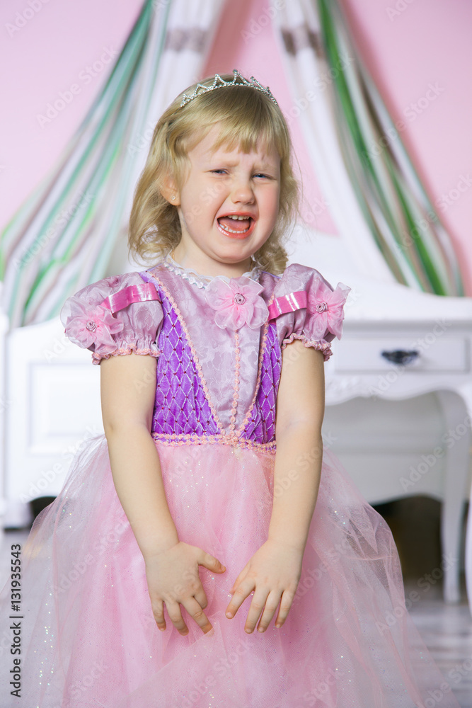Little unhappy princess girl in pink dress and crown in her royal room ...