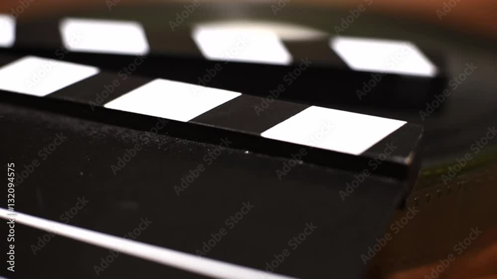 Movie clapper board detail placed on big film reel on brown table ...