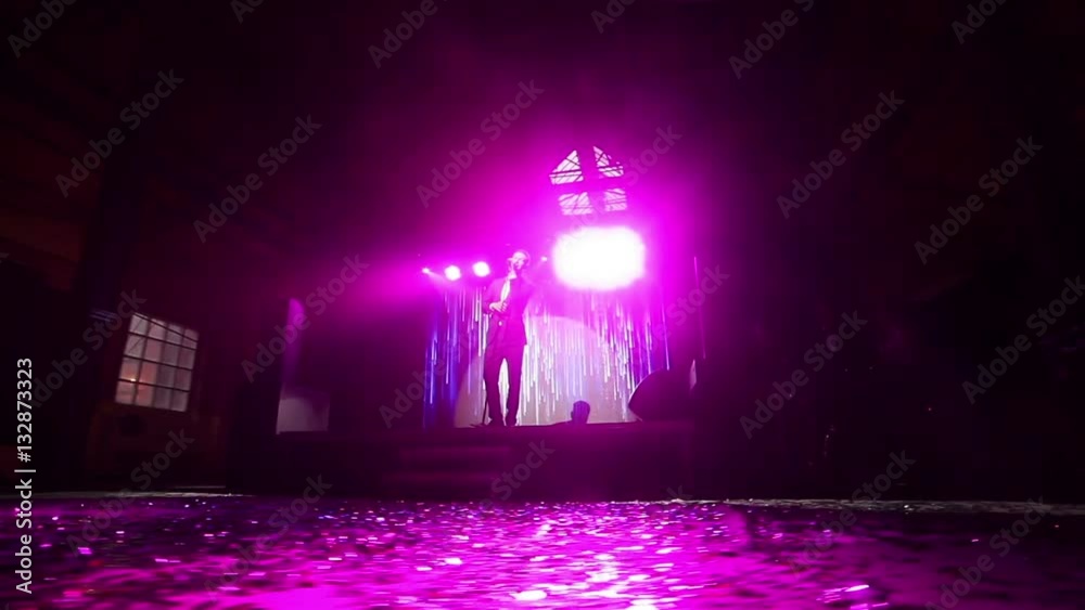 Silhouetted man sings on light decorated concert stage floor POV low ...