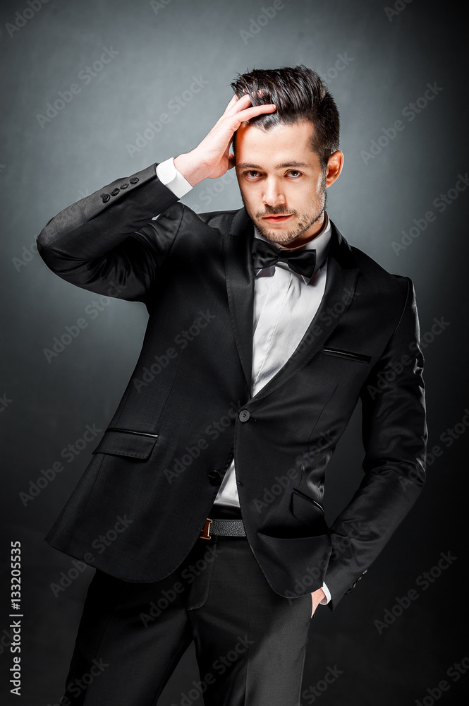 portrait of confident handsome man in black suit with bowtie posing in ...