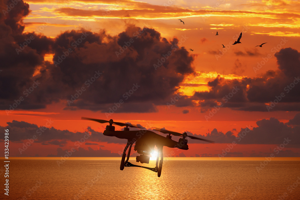 Silhouette of flying drone in glowing red sunset sky above sea Stock ...