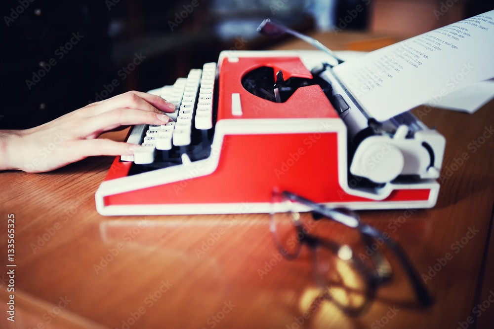 Women's hands are printed on a typewriter in red close-up. Writing ...