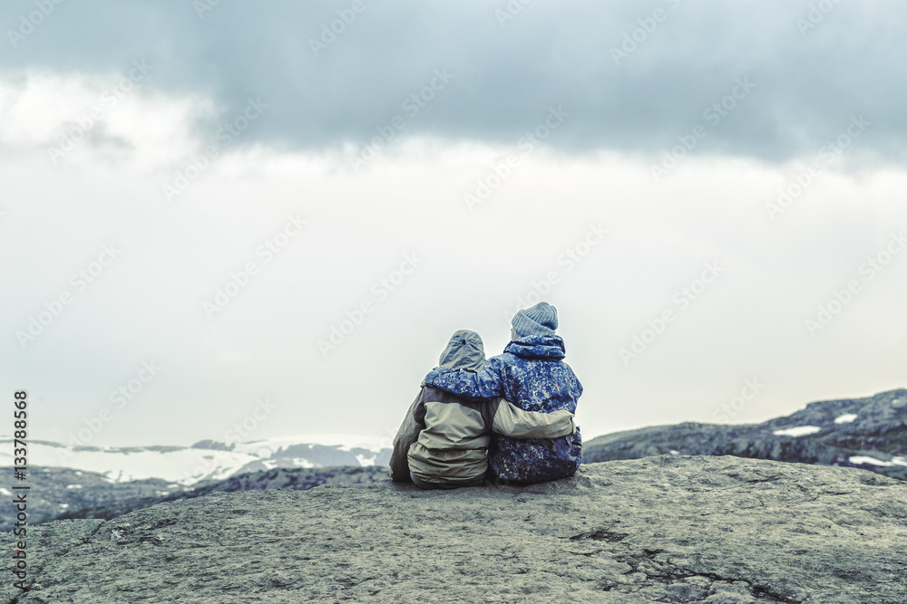 Boy and girl romantic couple sit hugging, embracing at edge of cliff ...