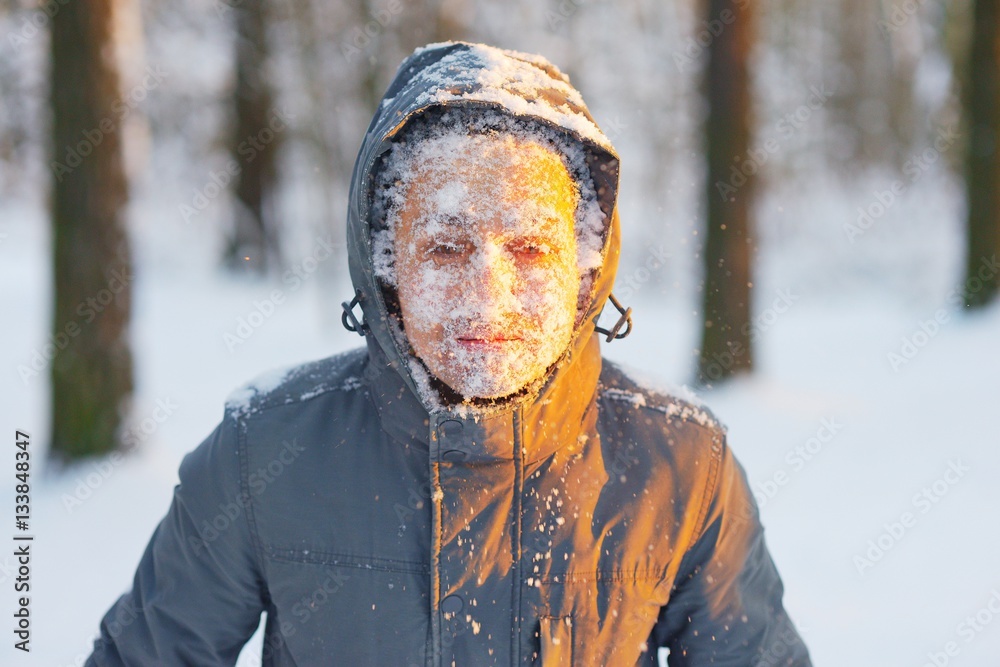 Frozen young man in a jacket with a hood, covered with snow in winter ...