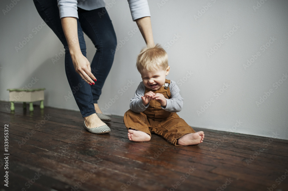 Low section of mother standing near baby boy sitting on floor at home ...