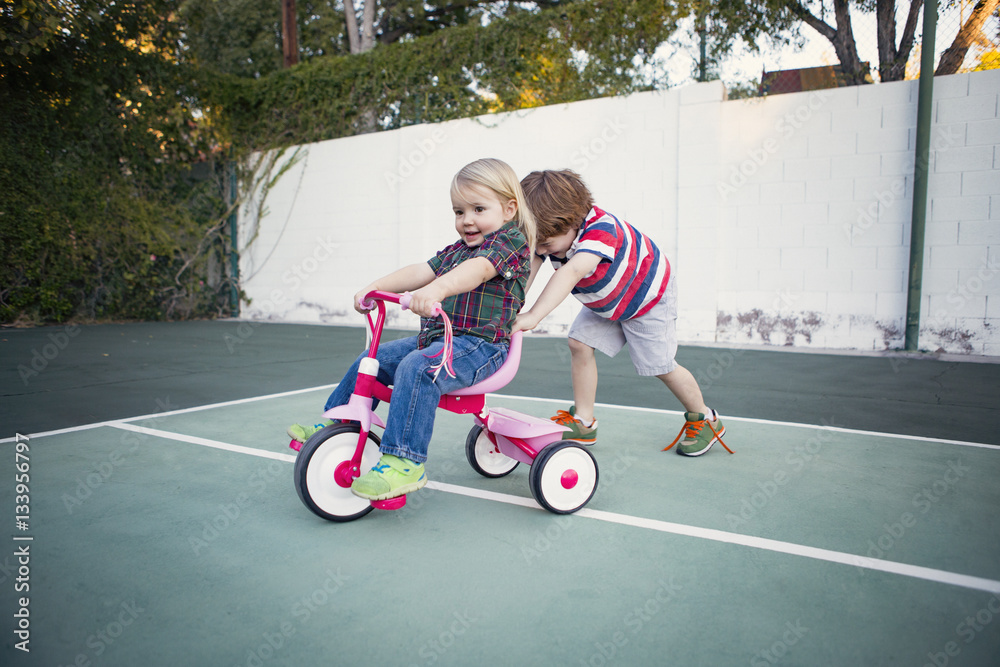 Boy pushing sister sitting on tricycle at yard Stock Photo | Adobe Stock