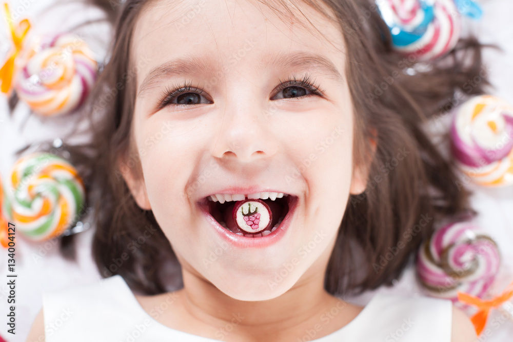 Pretty girl among the sweets, candies and lollipops. Funny child with ...