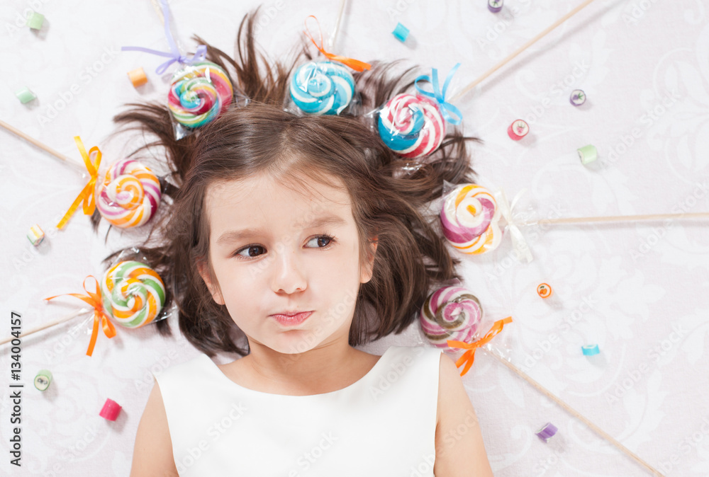 Pretty girl among the sweets, candies and lollipops. Funny child with ...