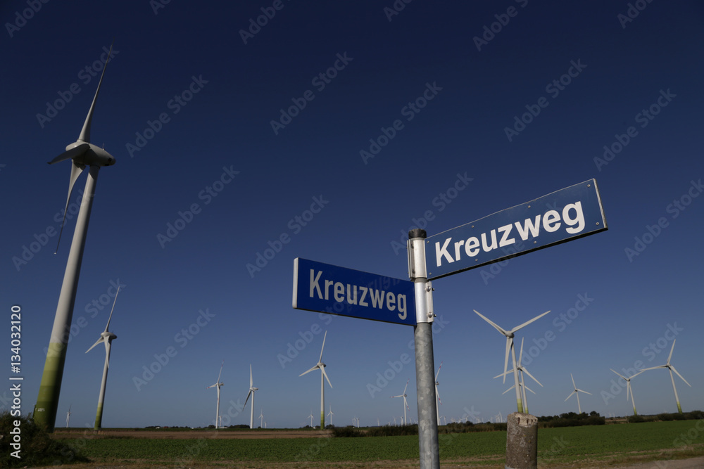 Strassenschild "Kreuzweg" und im hintergrund windräder und blauer ...
