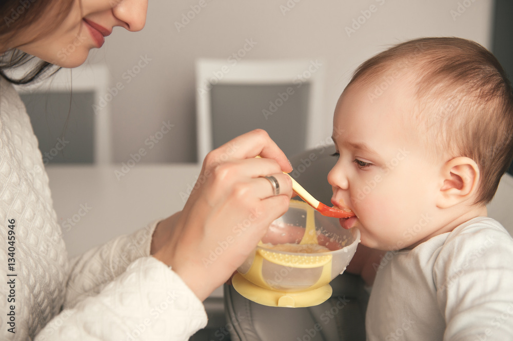 Mom feeding her baby girl with a spoon. Mother giving food to her eight ...