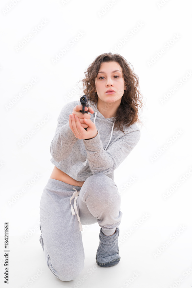 Young girl in a tracksuit with a gun. Beautiful young woman is aiming a ...