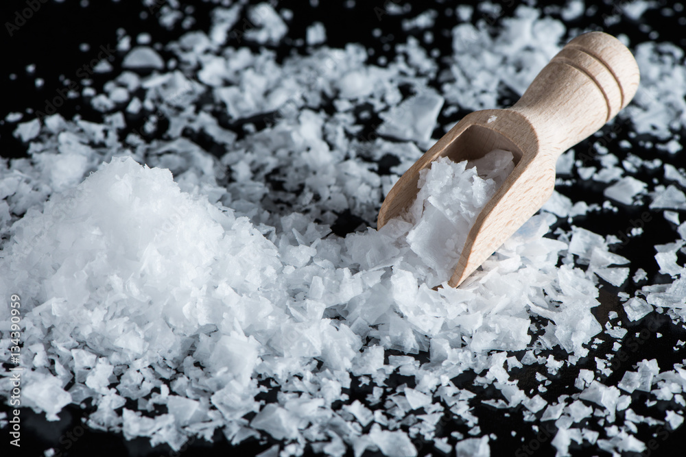 Salt flakes and wooden scoop on black background Stock Photo | Adobe Stock