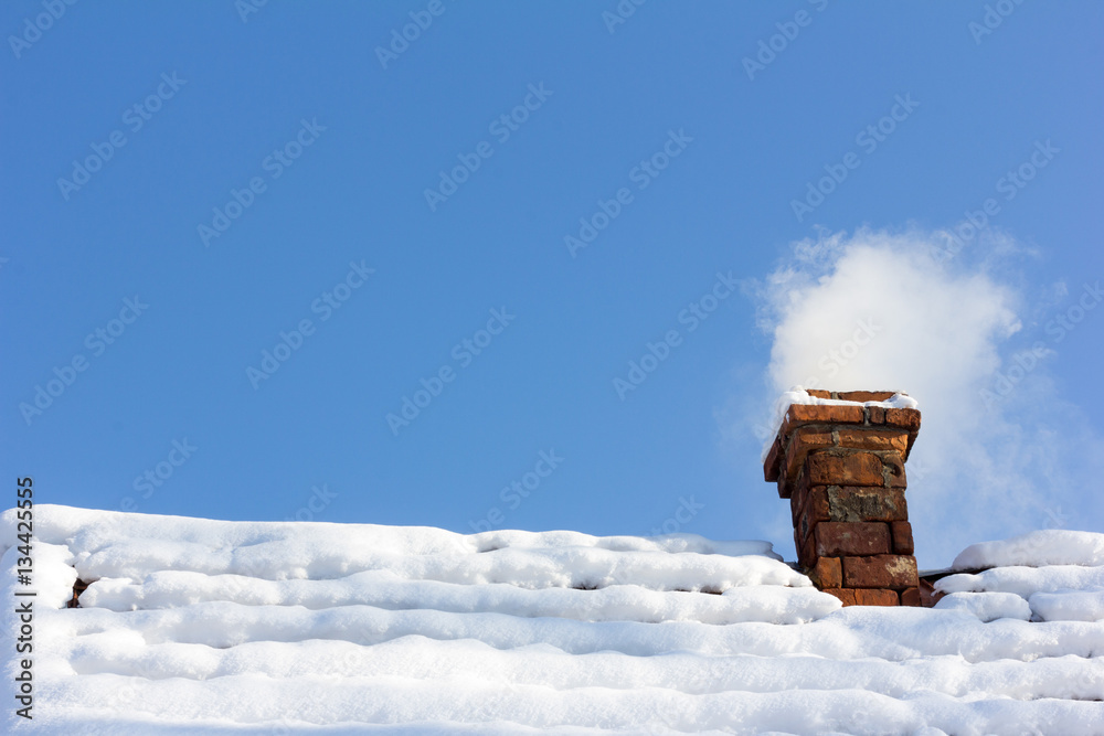 smoke out of a brick chimney on a snowy rooftop on the background of ...