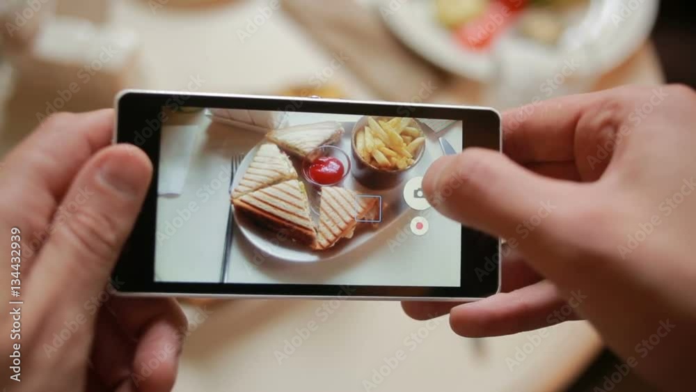 Trendy man in a restaurant make photo of food with mobile phone camera ...