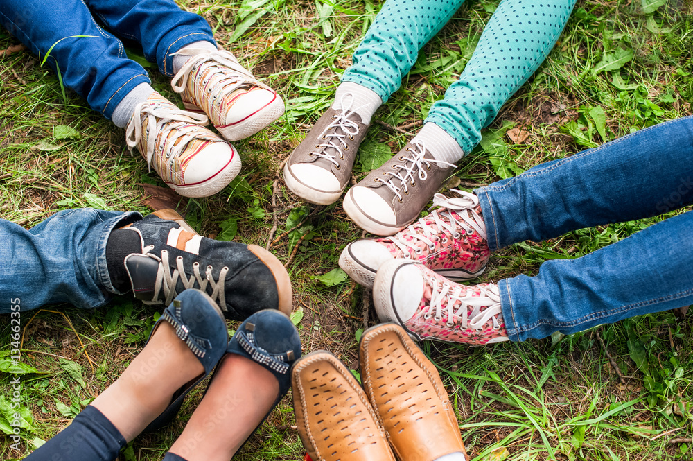 A group of friends sitting on the green grass make foot circle with ...