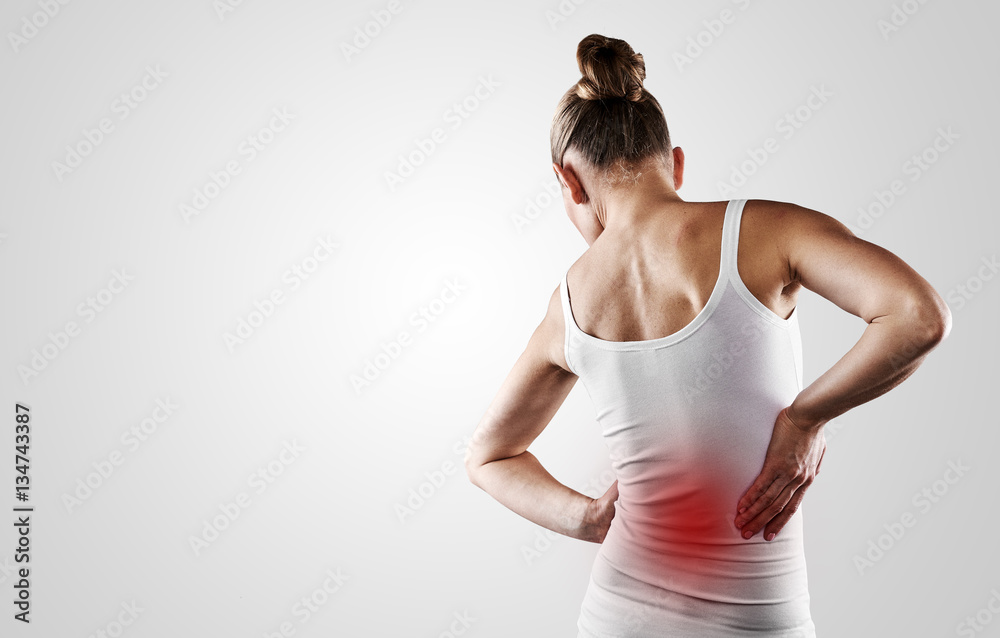 Portrait of young woman touching her painful back over grey background ...